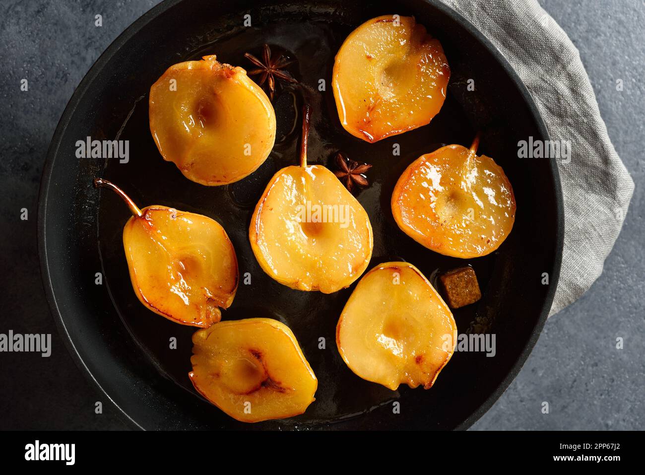 Vanilla poached pears in pan over dark stone background. Top view, flat ...