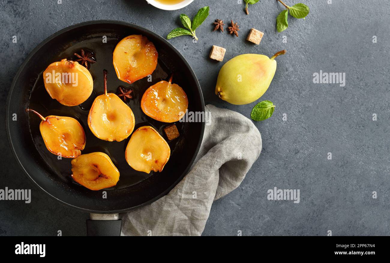 Vanilla poached pears in pan over dark stone background with copy space ...