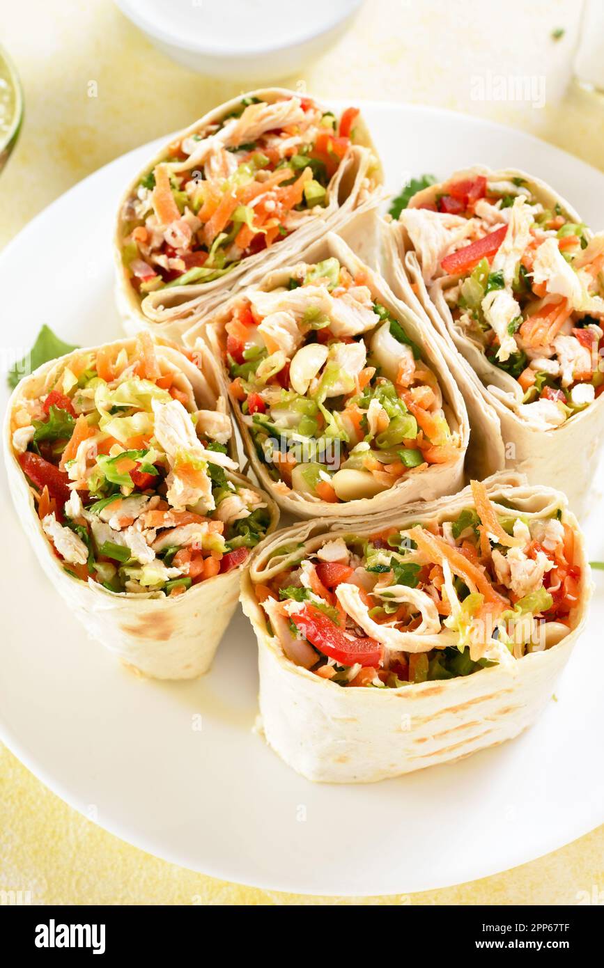 Tortilla wraps with chicken and fresh vegetables on plate over light ...