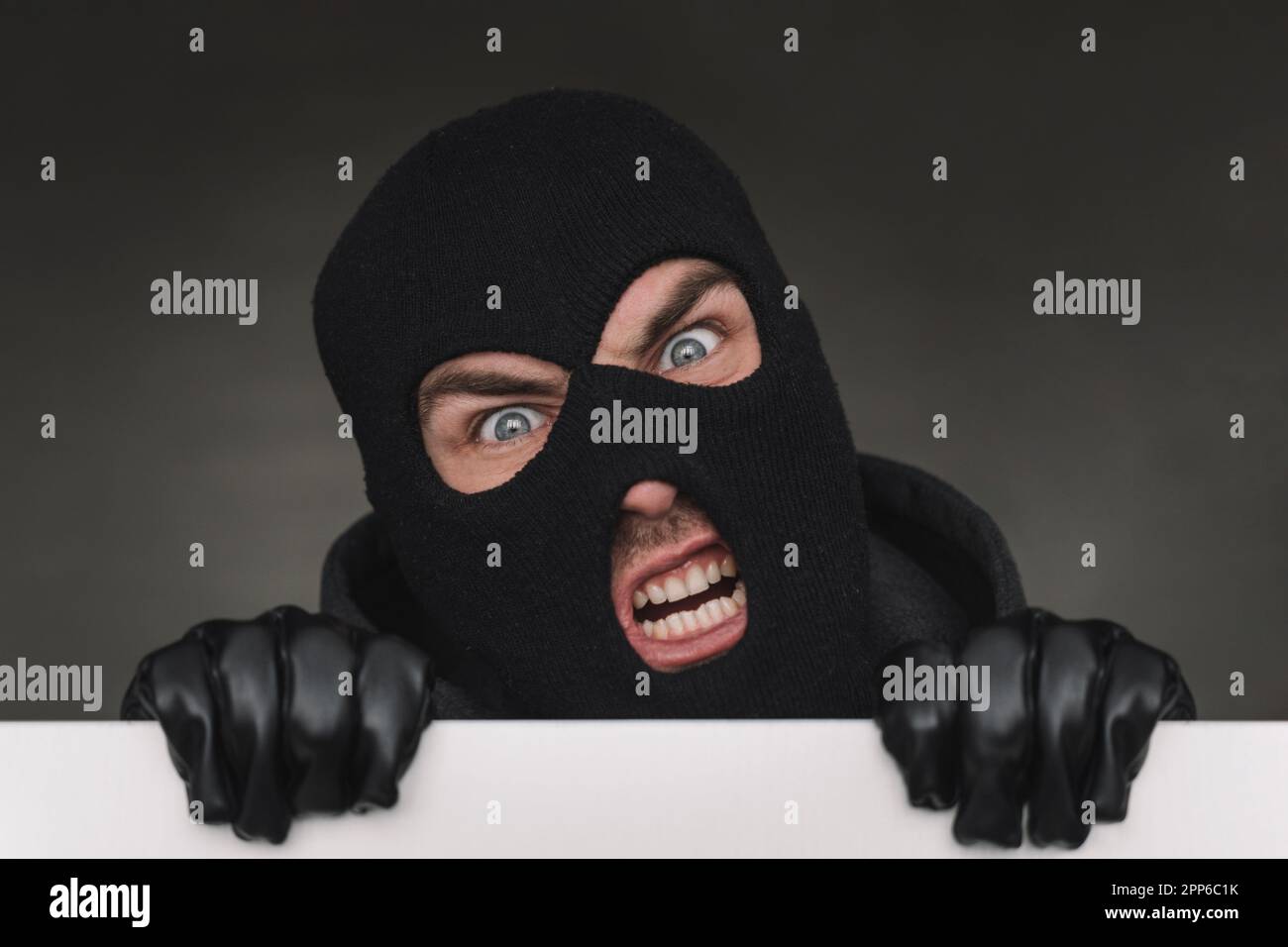 An evil thief in a mask looks out from behind a white board. an evil ...