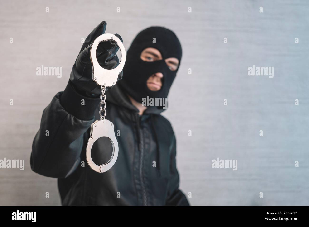 a bandit in a black mask and gloves with handcuffs in his hands on a ...