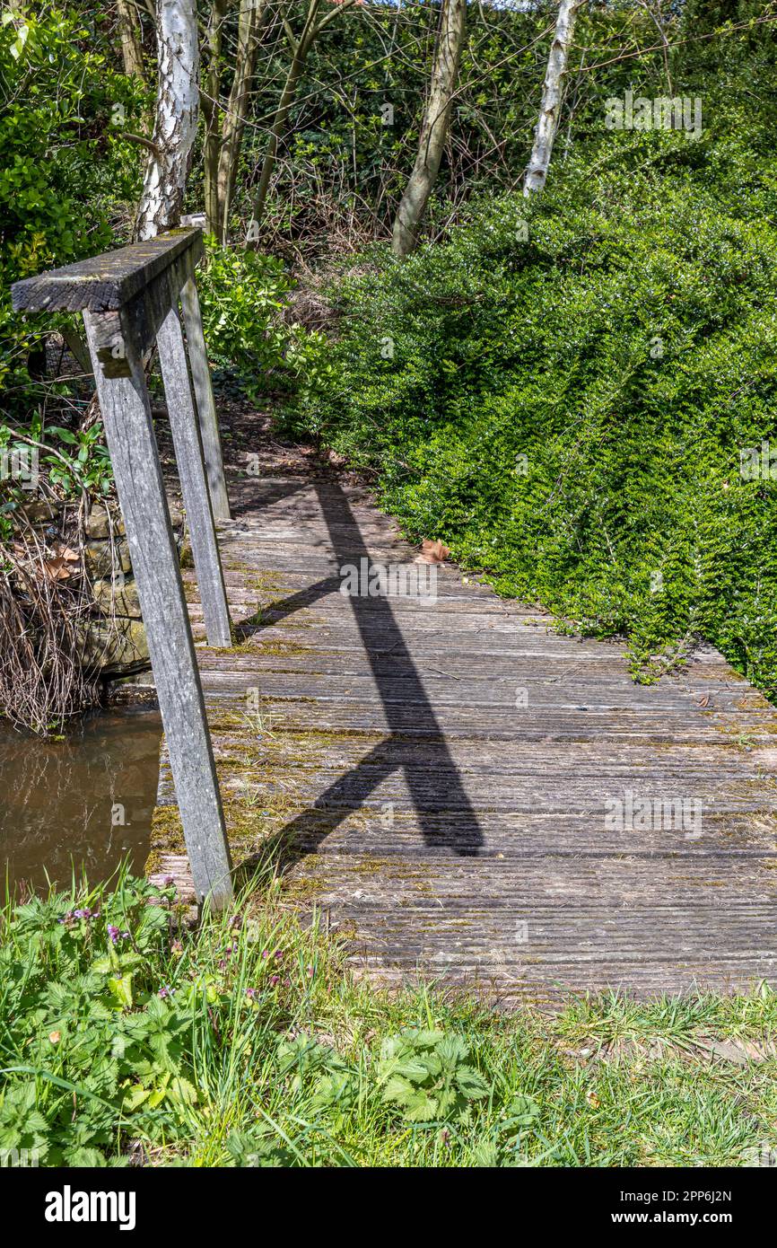 Old and worn small simple wooden bridge over a stream, sloping fence ...