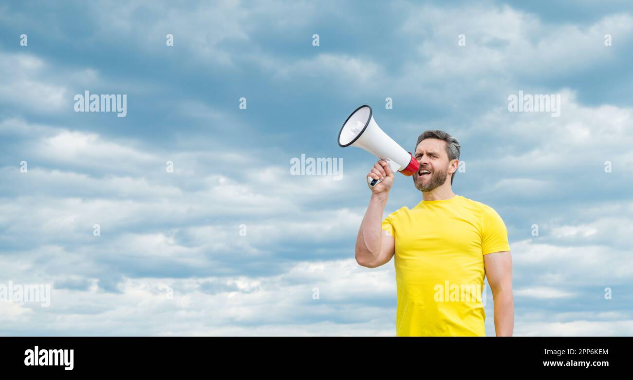 man in yellow shirt shout in loudspeaker on sky background with copy ...