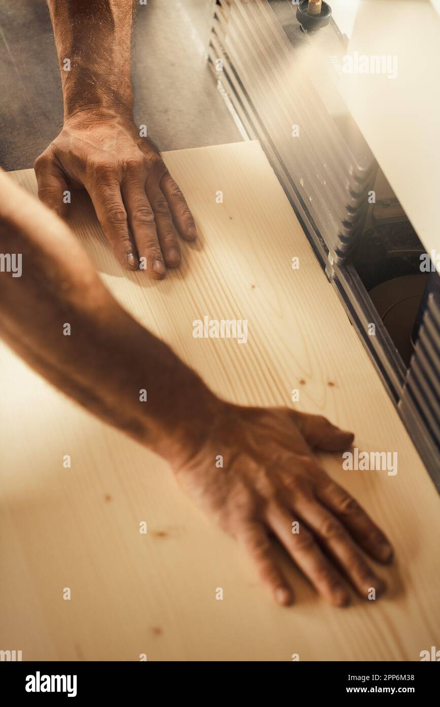 Strong carpenter's hands hold, guide, restrain, push, and move lumber ...