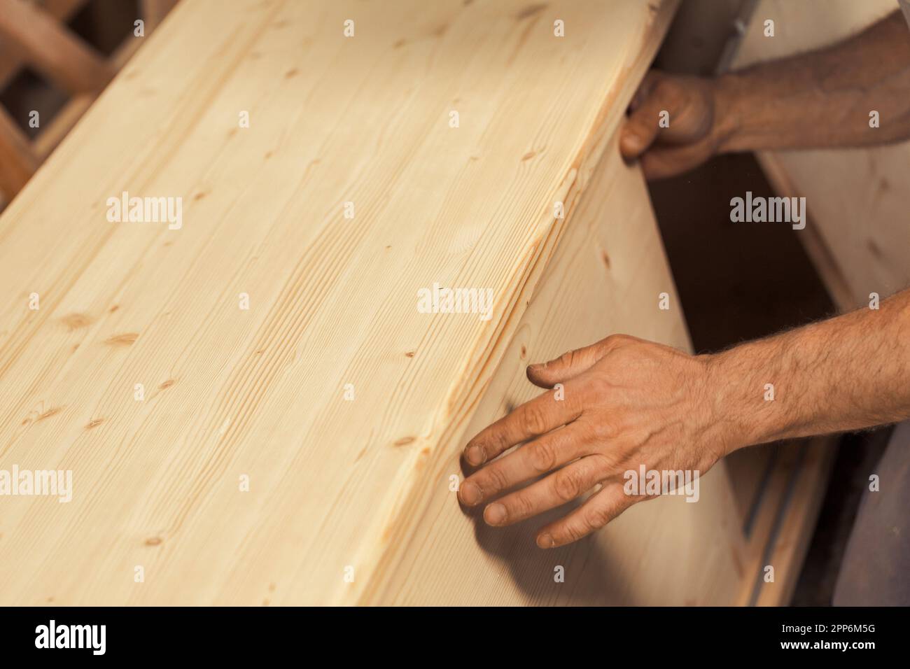 Strong carpenter's hands hold, guide, restrain, push, and move lumber ...