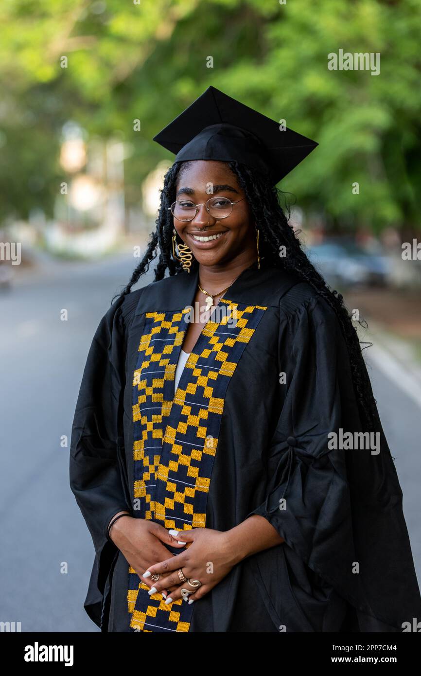 Portrait, Black African Female University Graduate wearing black gown and cap, proud of academic ...