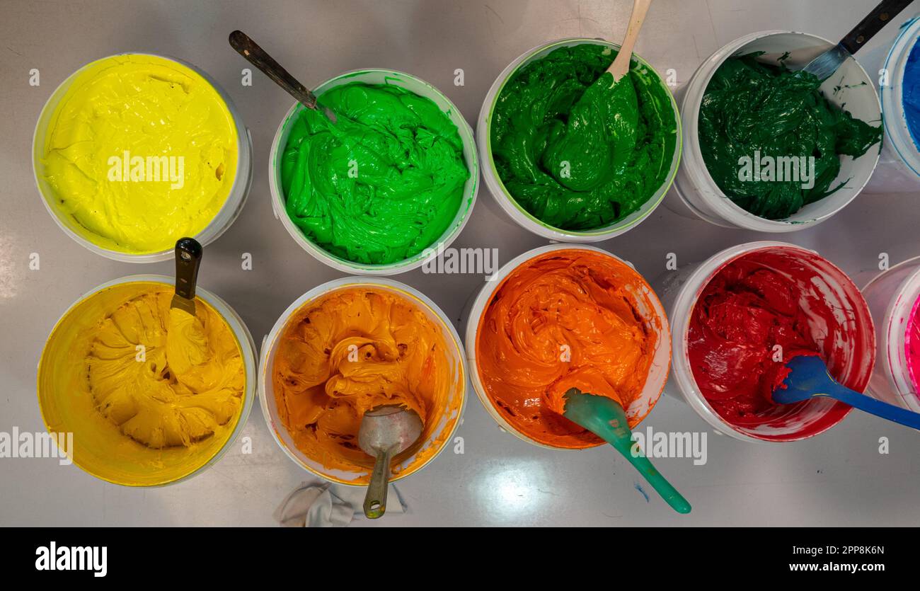 Top view, colorful fabric printing inks in white buckets. Stirring the ...
