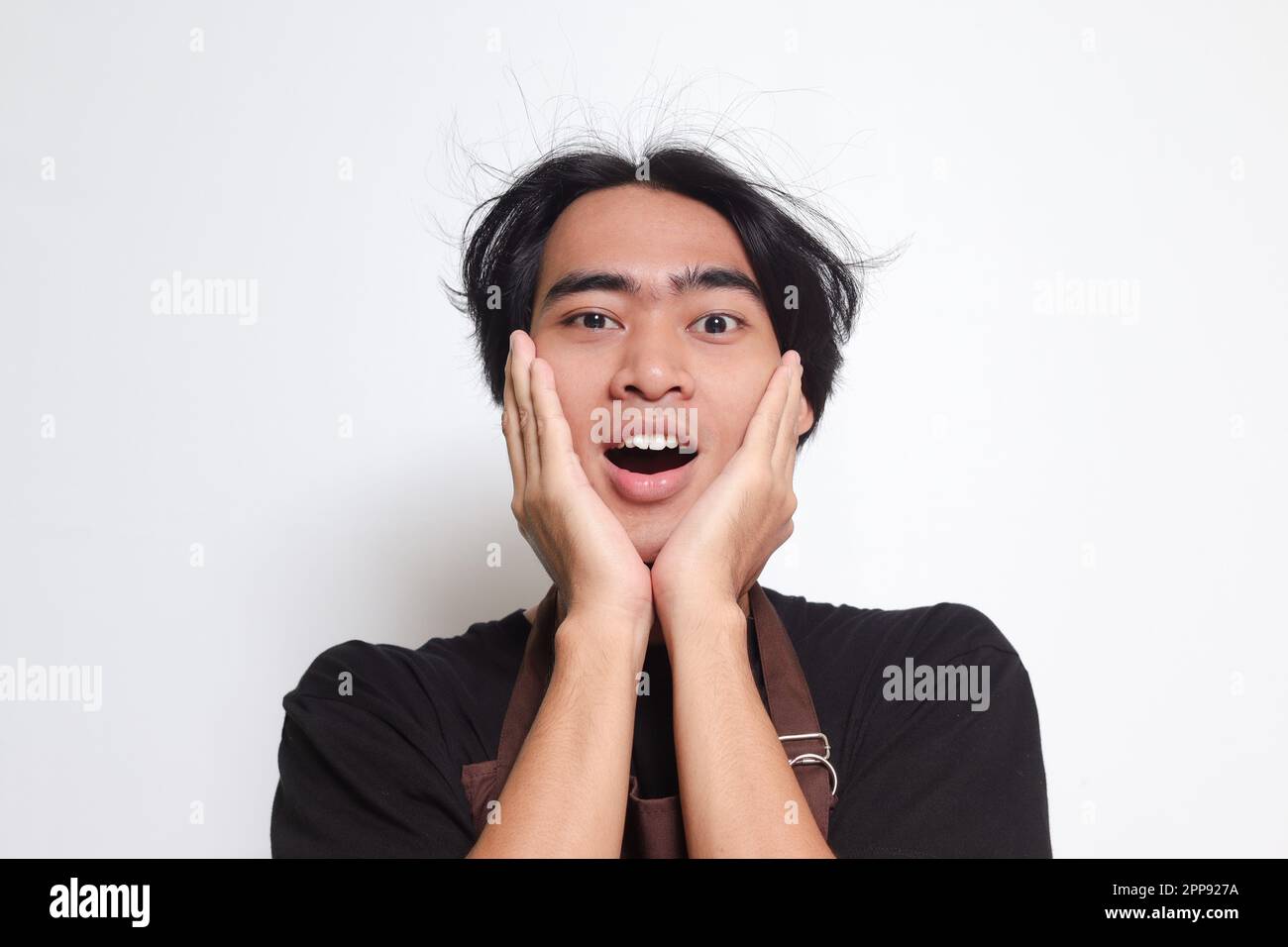 Close up portrait of shocked Asian barista man in brown apron holding ...