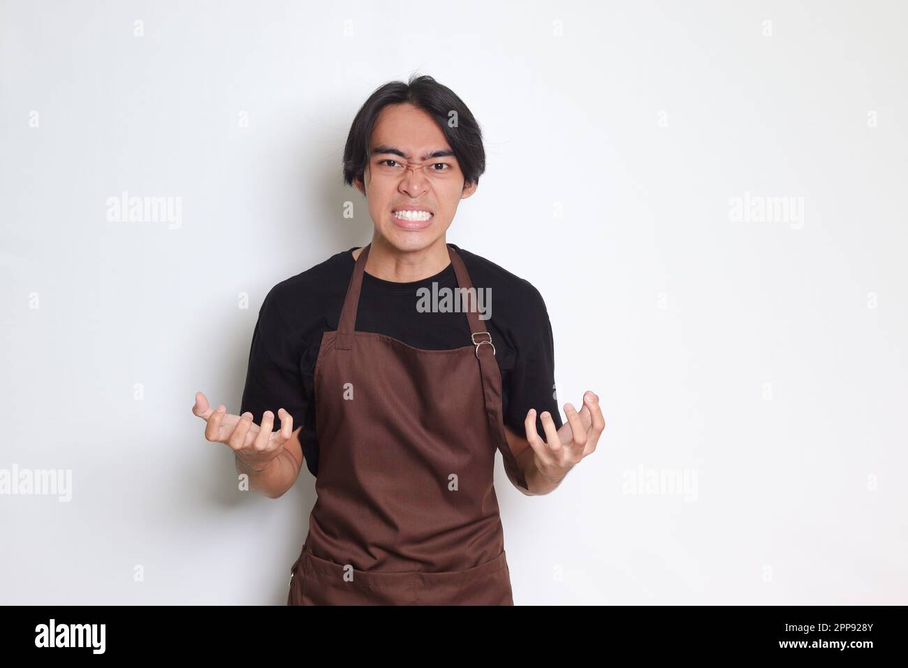 Portrait of annoyed Asian barista man in brown apron making angry hand ...