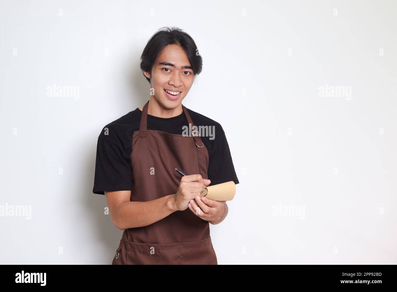 Portrait of attractive Asian barista man in brown apron taking order ...
