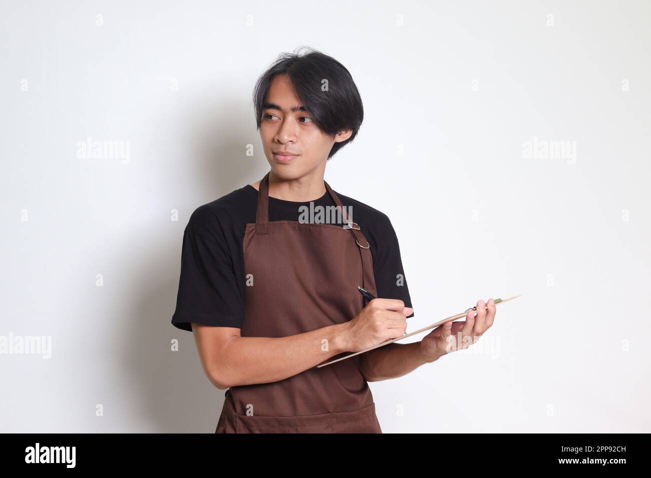 Portrait of attractive Asian barista man in brown apron taking order ...