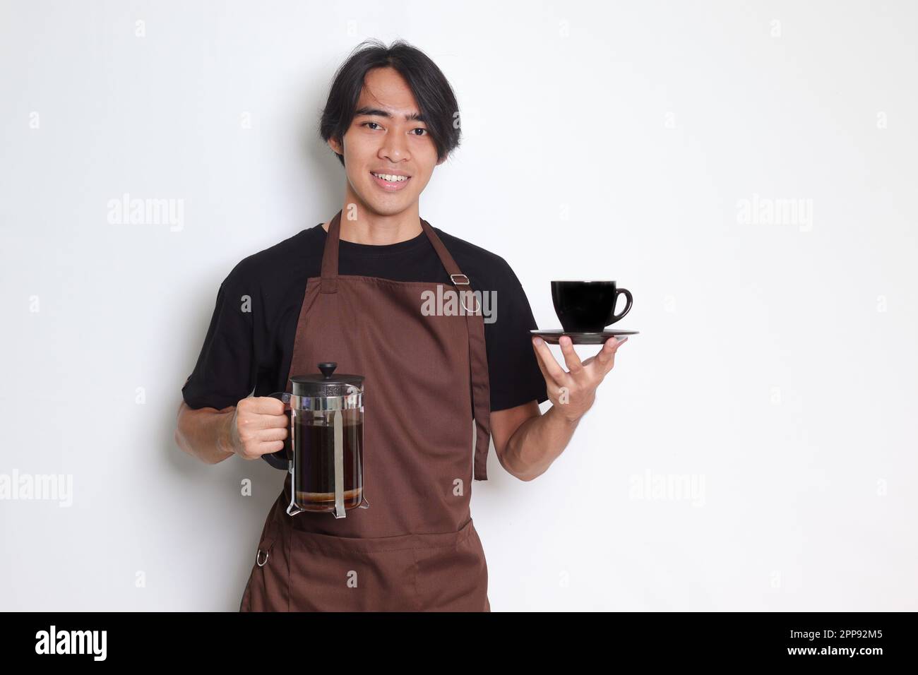 Portrait of attractive Asian barista man in brown apron showing a cup ...