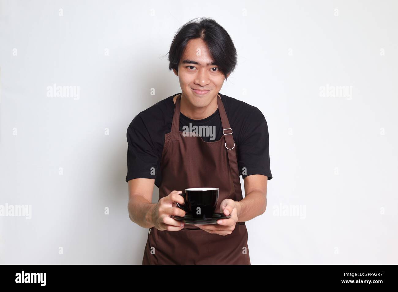 Portrait of attractive Asian barista man in brown apron serving a cup ...