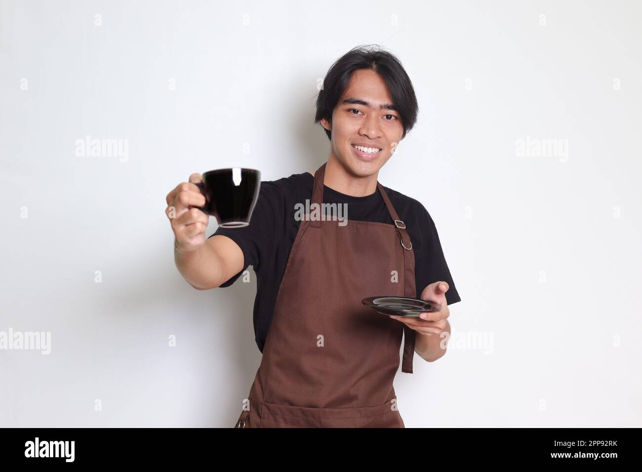 Portrait of attractive Asian barista man in brown apron serving a cup ...