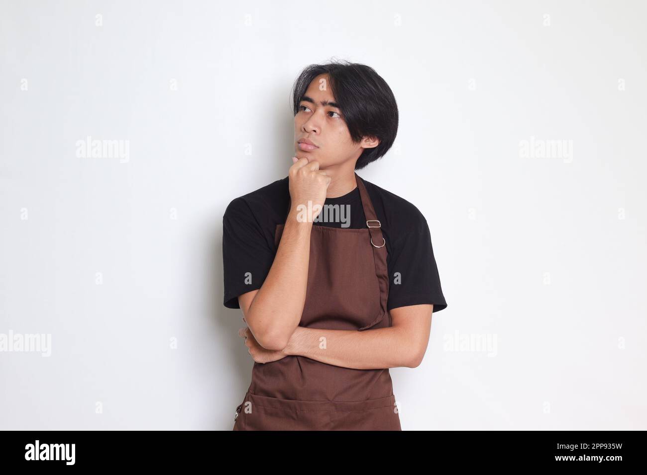 Portrait of attractive Asian barista man in brown apron thinking about ...