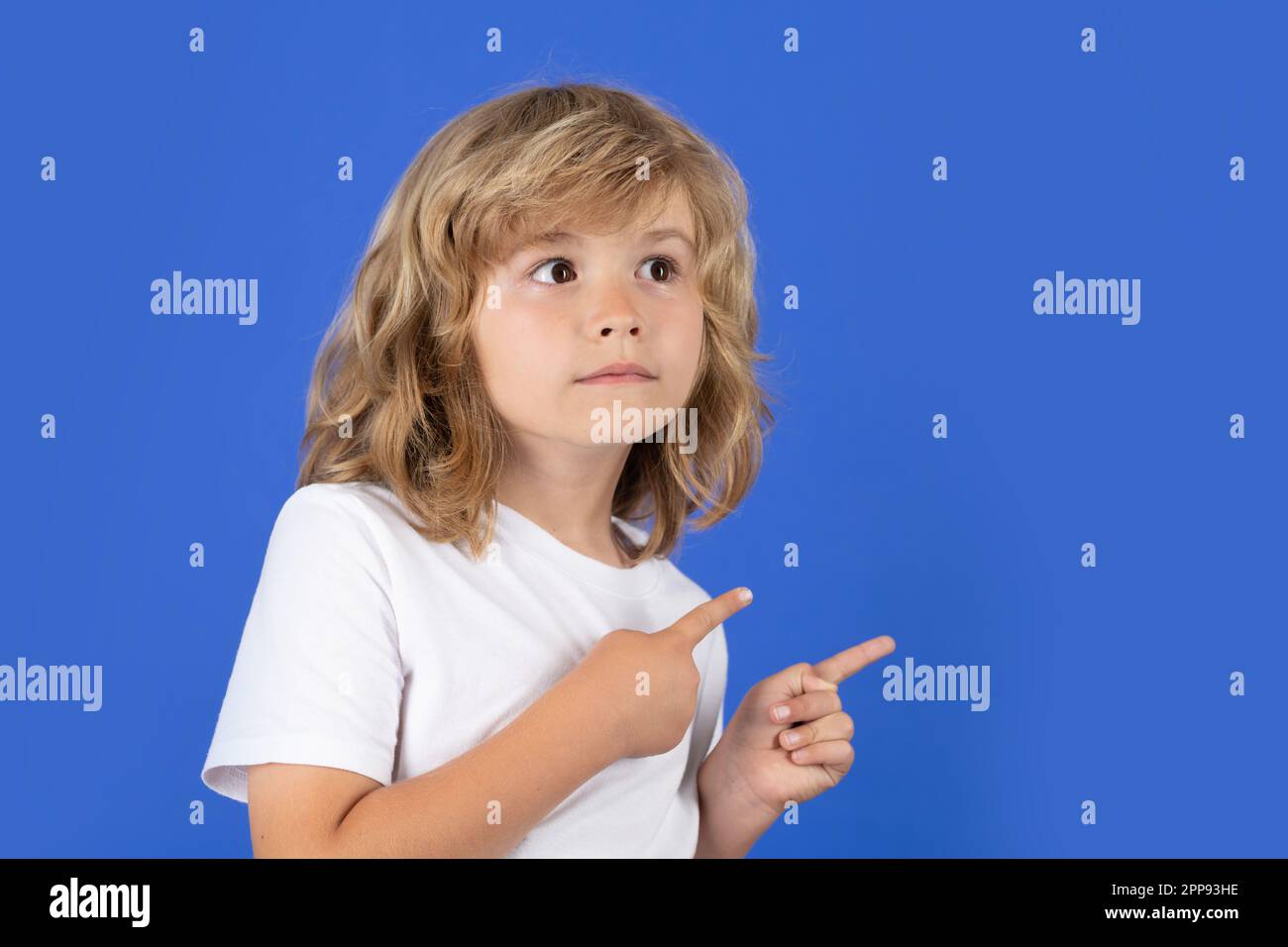 Child looking away, pointing finger on blue isolated studio background ...