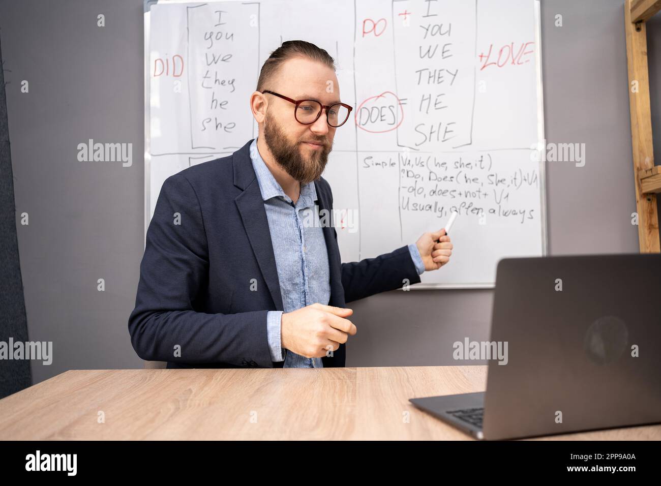 Teacher giving online English lesson sitting at table in classroom at ...