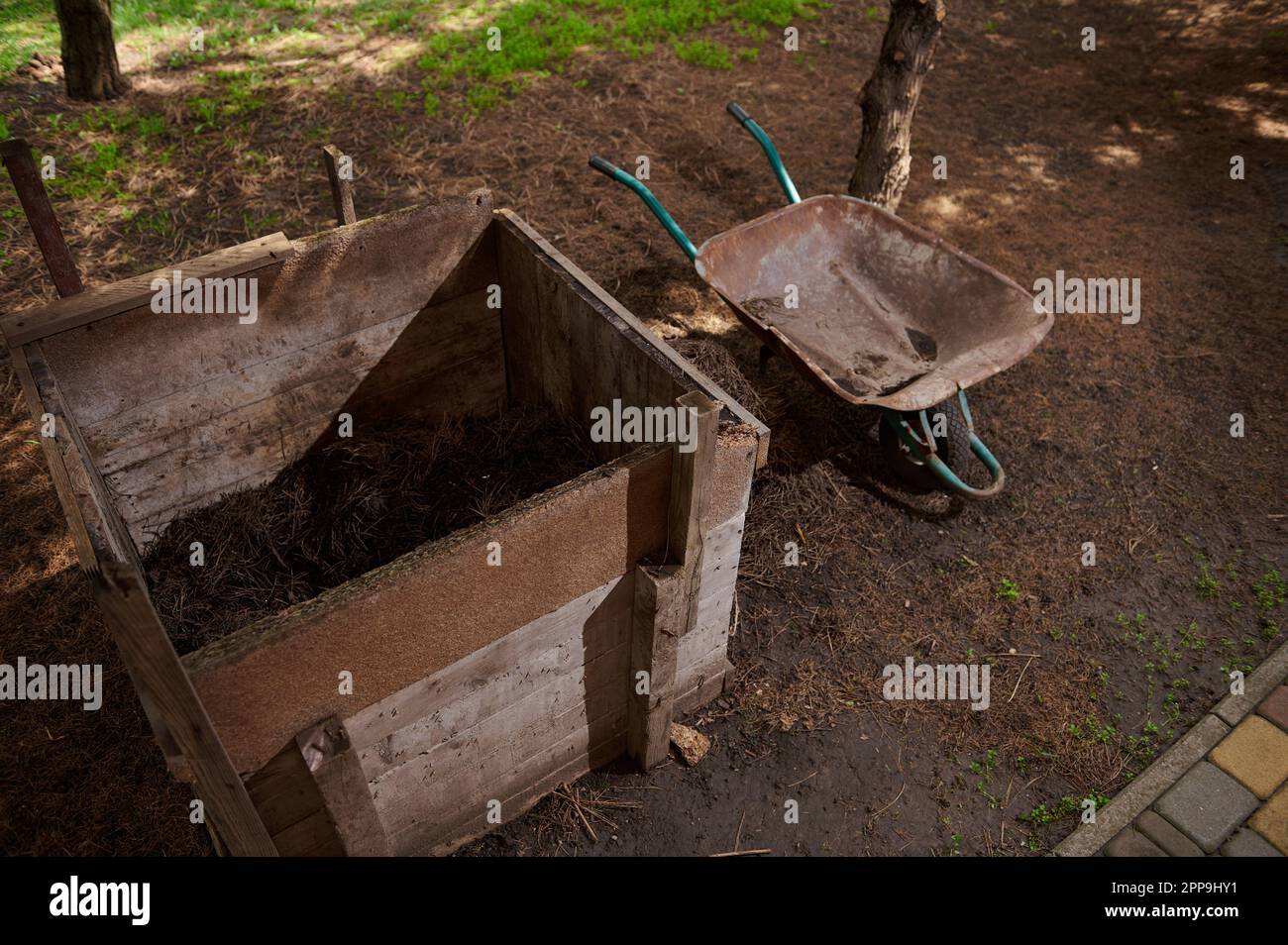 Still life with a wheelbarrow standing near a compost pit in a garden ...