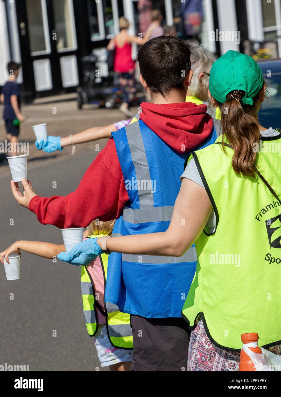 Helpers hold out plastic cups of water for runners in a 10k road race ...