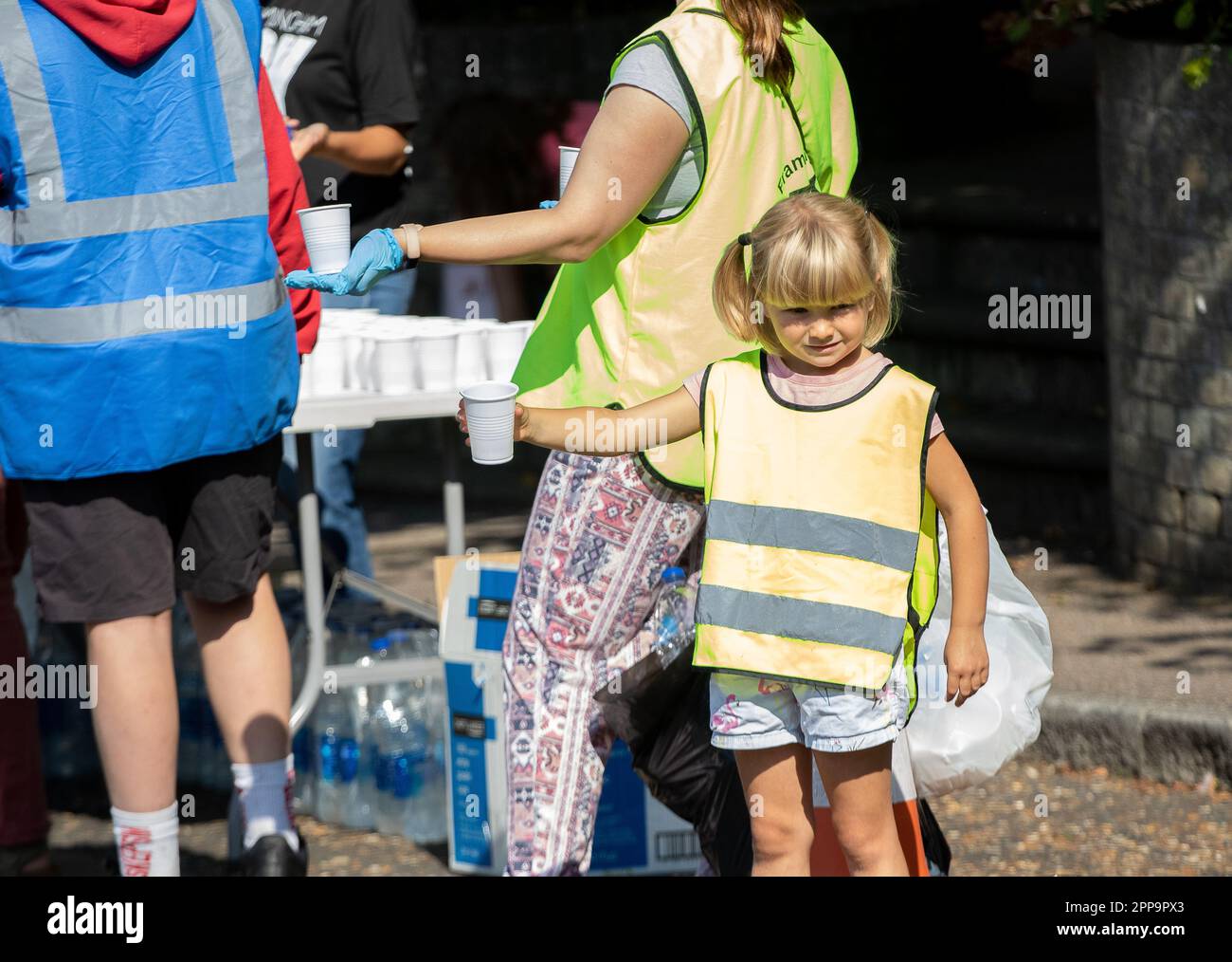 Very small girl with blond hair in bunches helps at a the water station ...