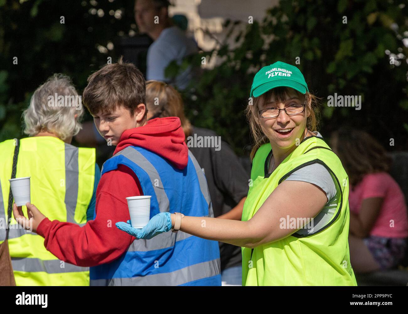 Helpers hold out plastic cups of water for runners in a 10k road race ...