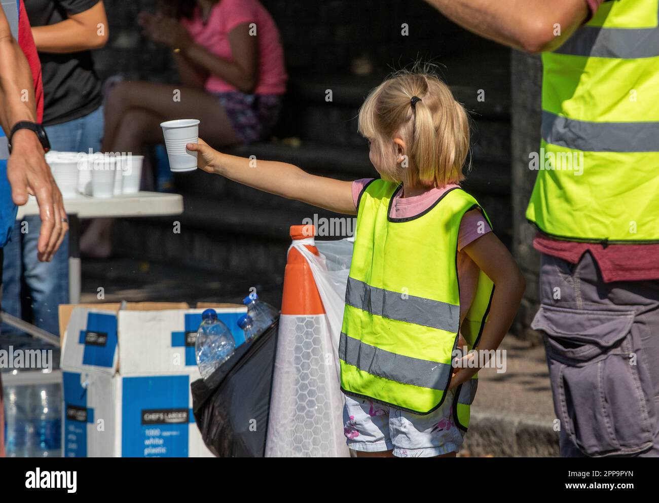 Very small girl with blond hair in bunches helps at a the water station ...
