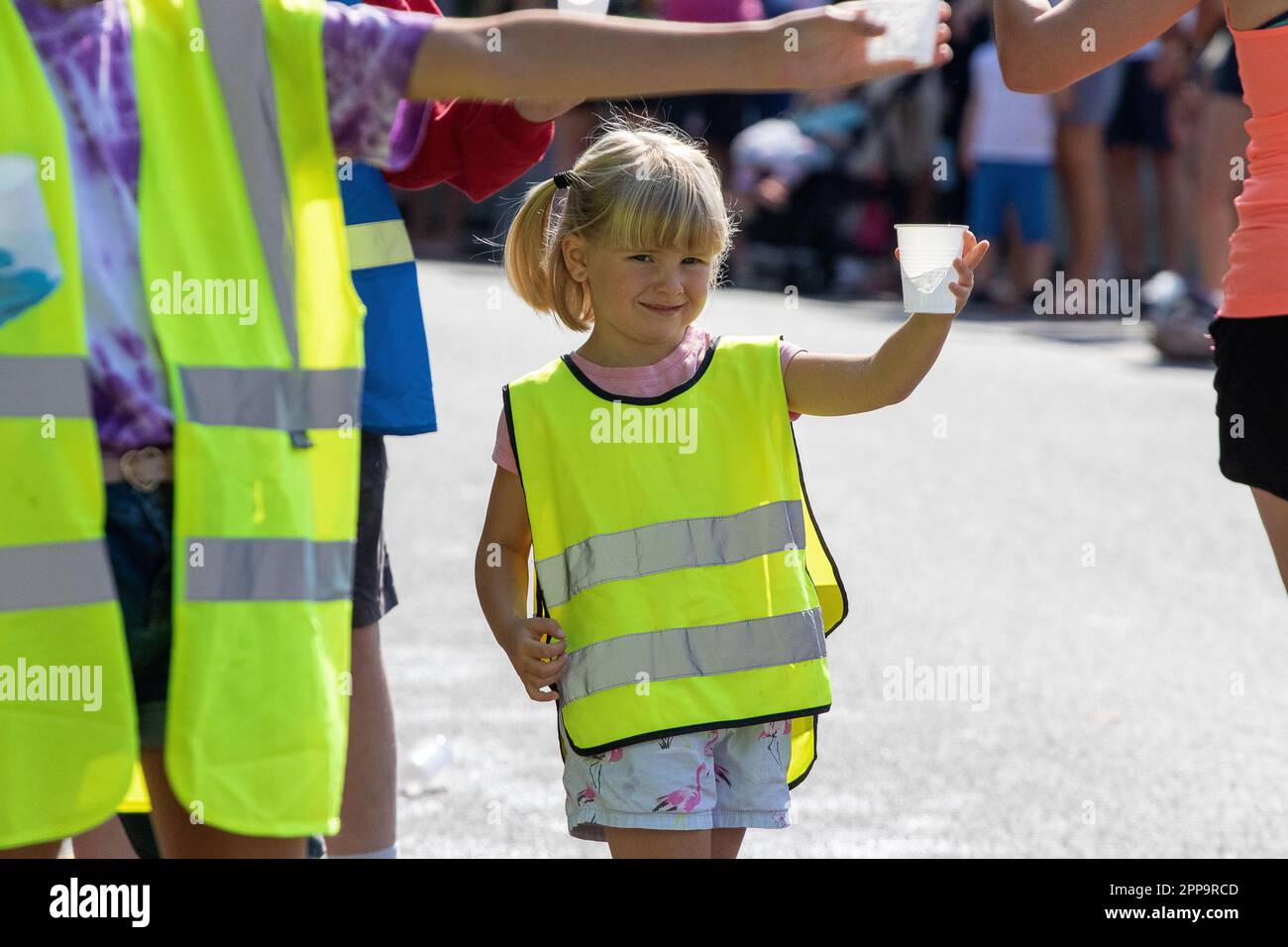 Very small girl with blond hair in bunches helps at a the water station ...