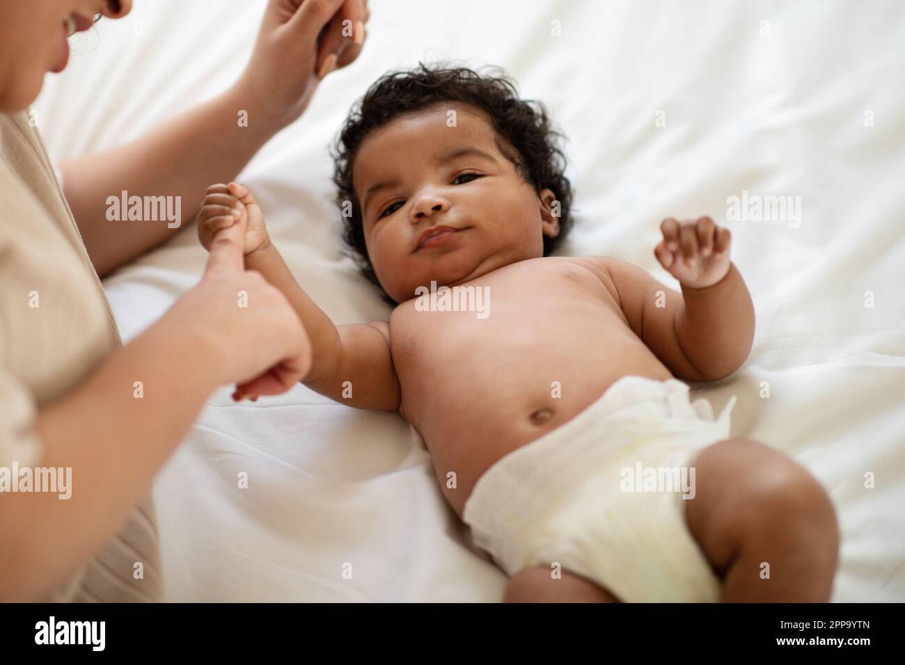Young african american lady looking at little baby in diaper, enjoys ...