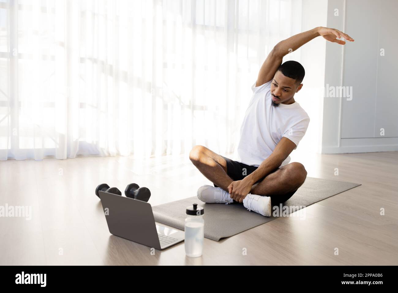 Sporty black guy stretching and watching fitness video on laptop Stock ...