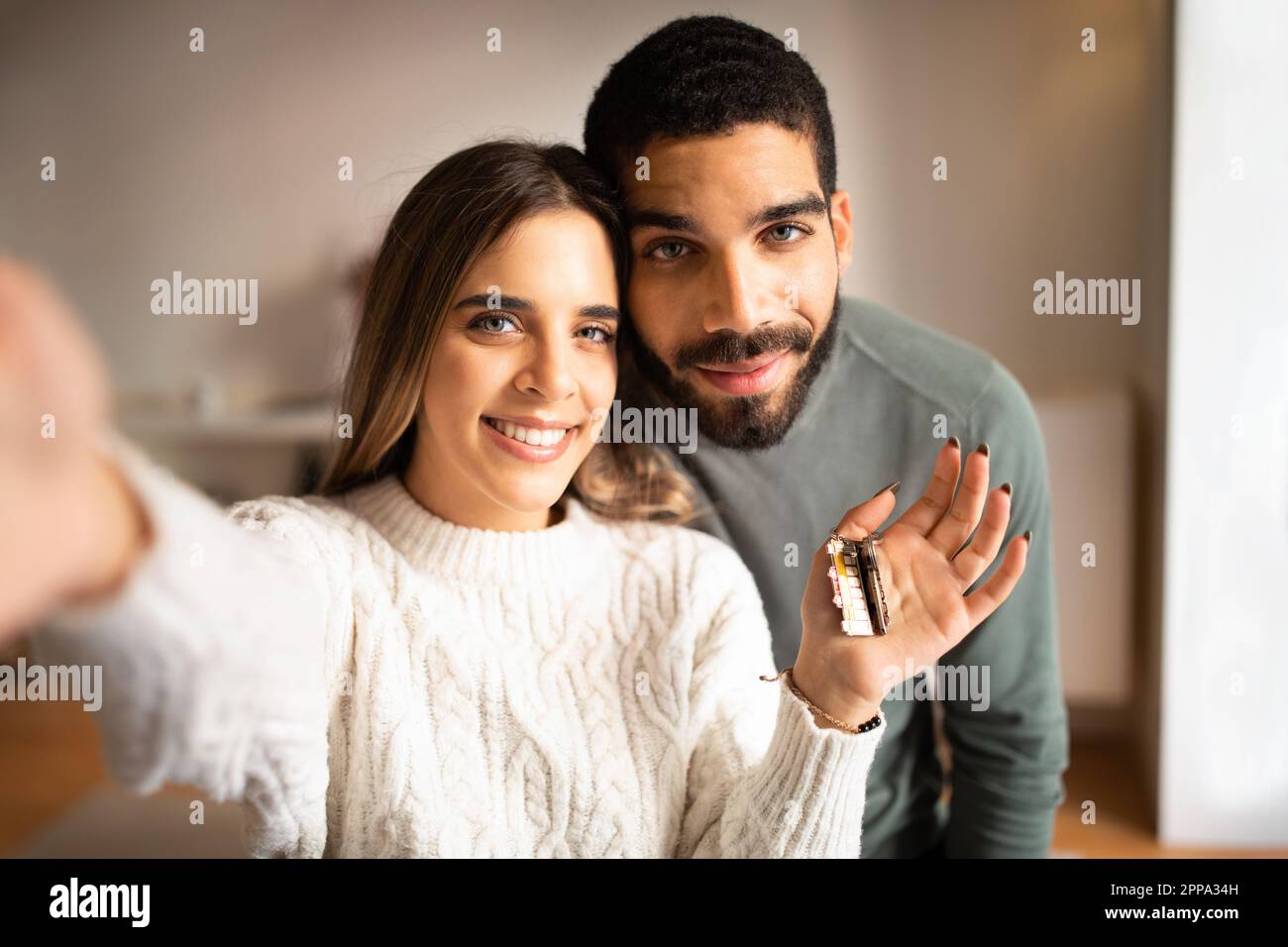 Glad millennial diverse male and wife take selfie together, shows keys from new apartment, enjoy ...