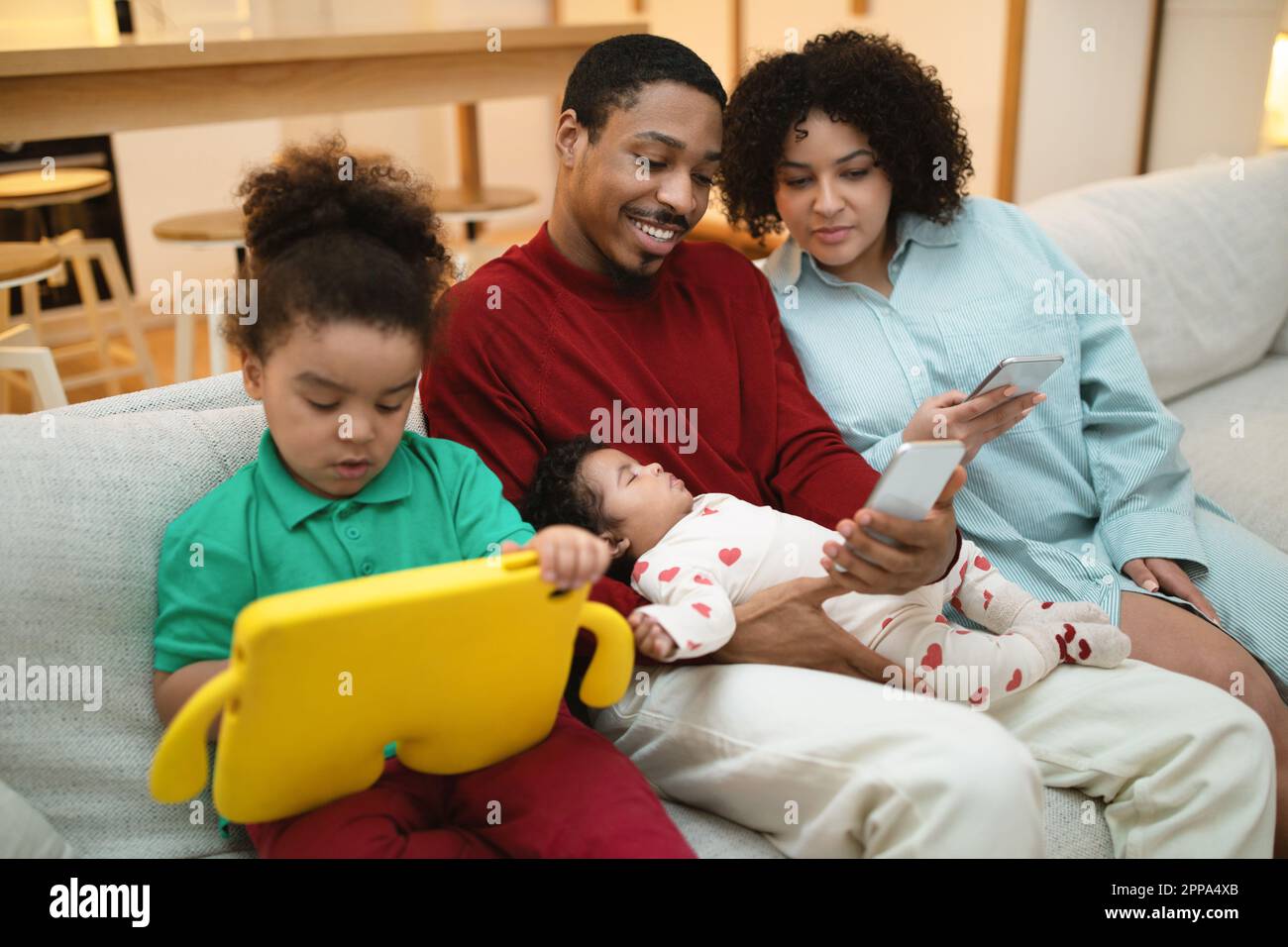 Happy loving multicultural family sitting on couch, using gadgets Stock ...