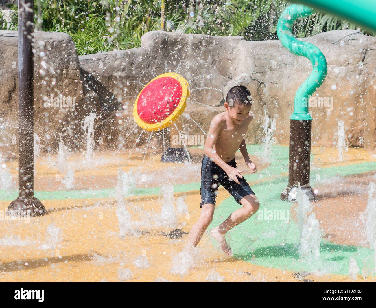 Asian child little boy having fun to play with water in park fountain ...