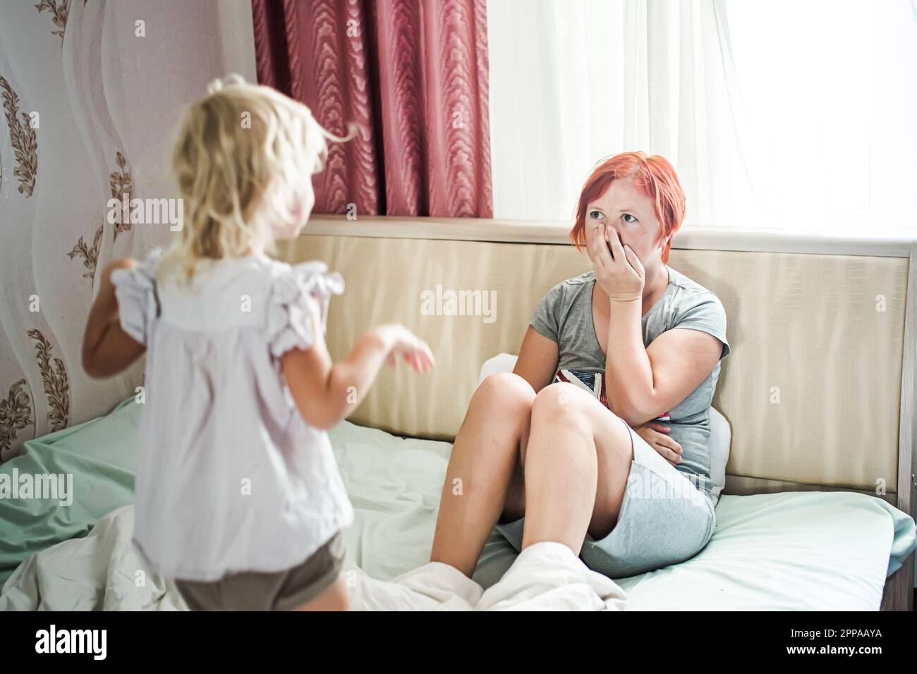 frightened mother looks at merry child. daughter plays near tired ...