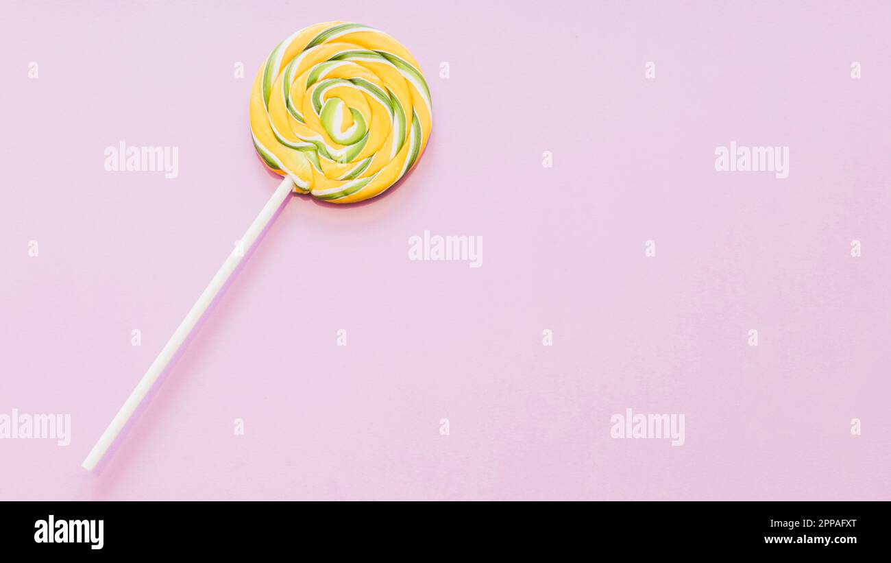 Yellow green striped lollipop against pink background Stock Photo - Alamy