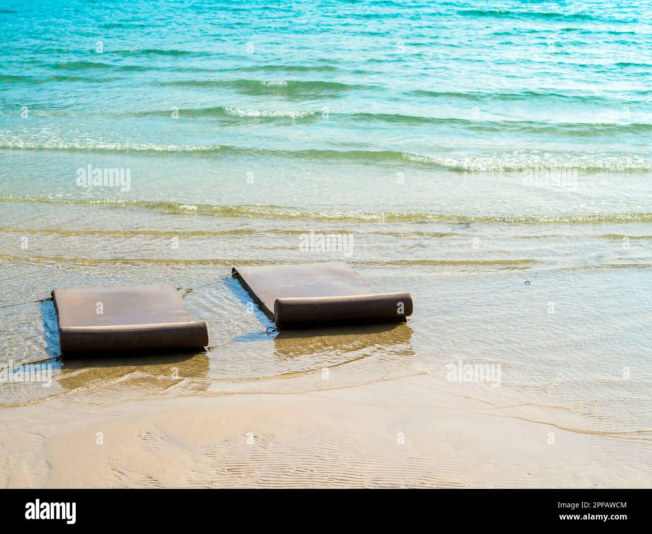 Two empty floating sunbed seats on the clean blue water sea wave and ...