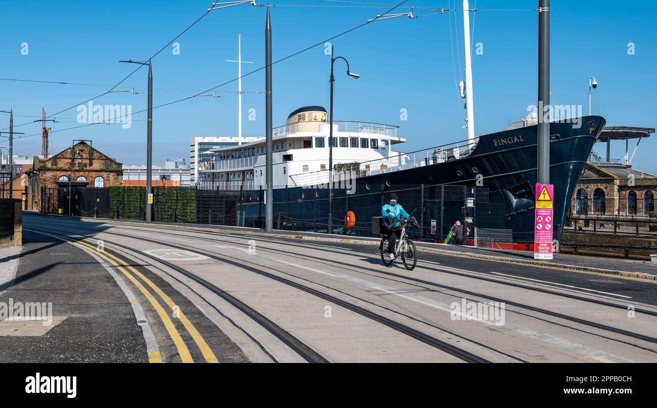 Cyclist riding on tram lines past Fingal Edinburgh floating hotel ship ...