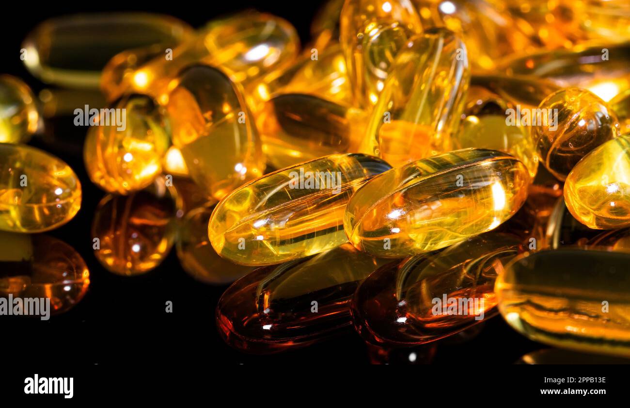 Macro Close up of Omega 3 gel capsule on a reflective black background ...