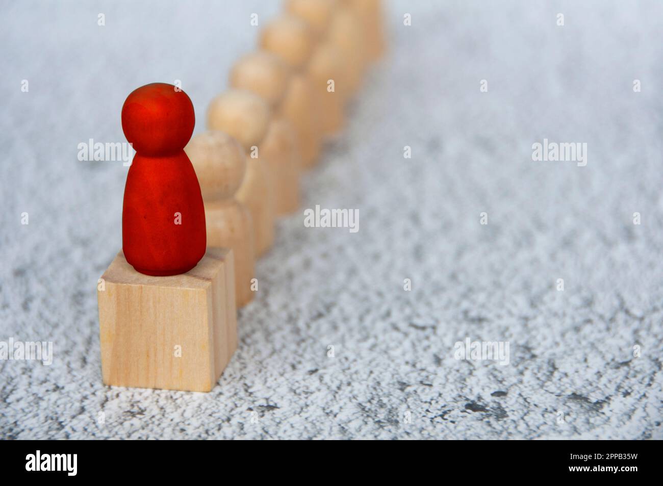 Red wooden figure on top of wooden block representing a leader leading ...