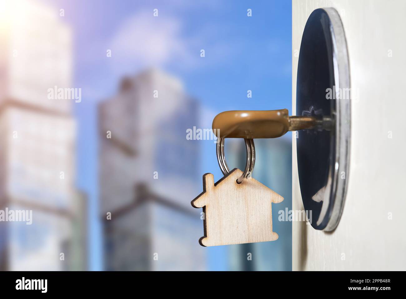 Key with a trinket in the form of a house in the door lock of an open ...