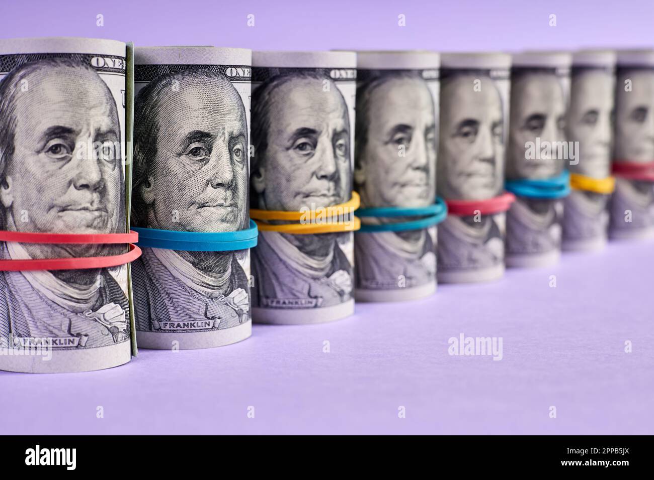 A row of rolled hundred dollar bills with rubber bands on purple ...