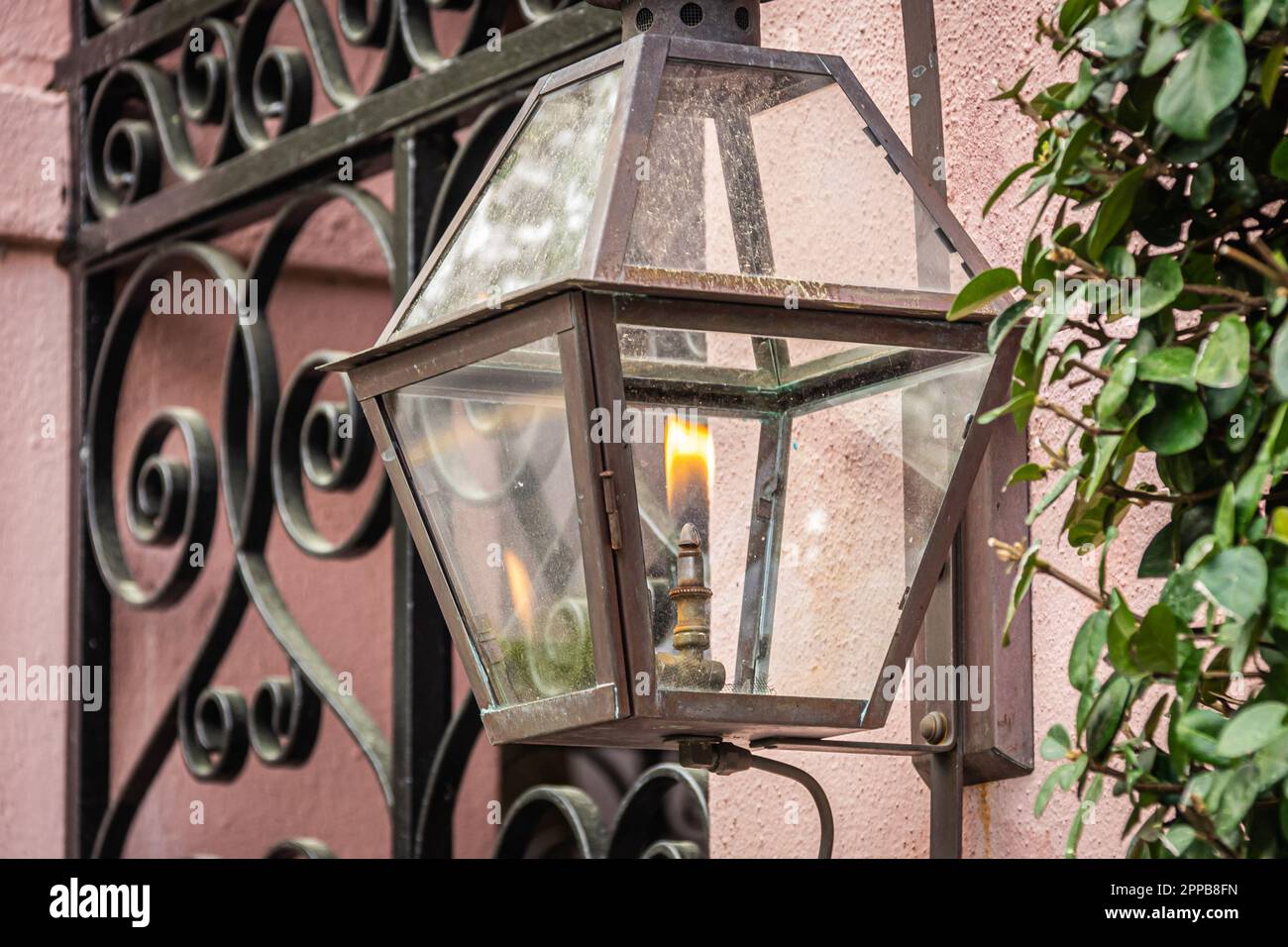 A close up of an old gas lamp that is lit in front of a pink home Stock ...