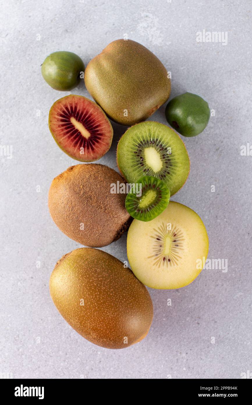 Different varieties of kiwi lie in a pile on the table. Halves of red ...