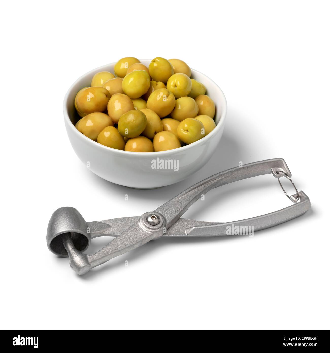 Bowl with green Turkish olives close up and a metal olive pitter and ...