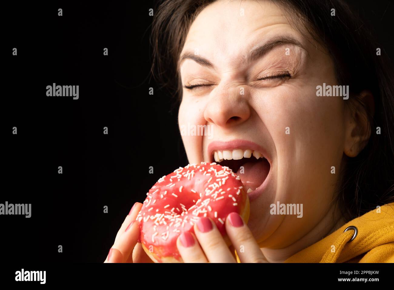 A woman bites a large red donut, a black background, a place for text ...