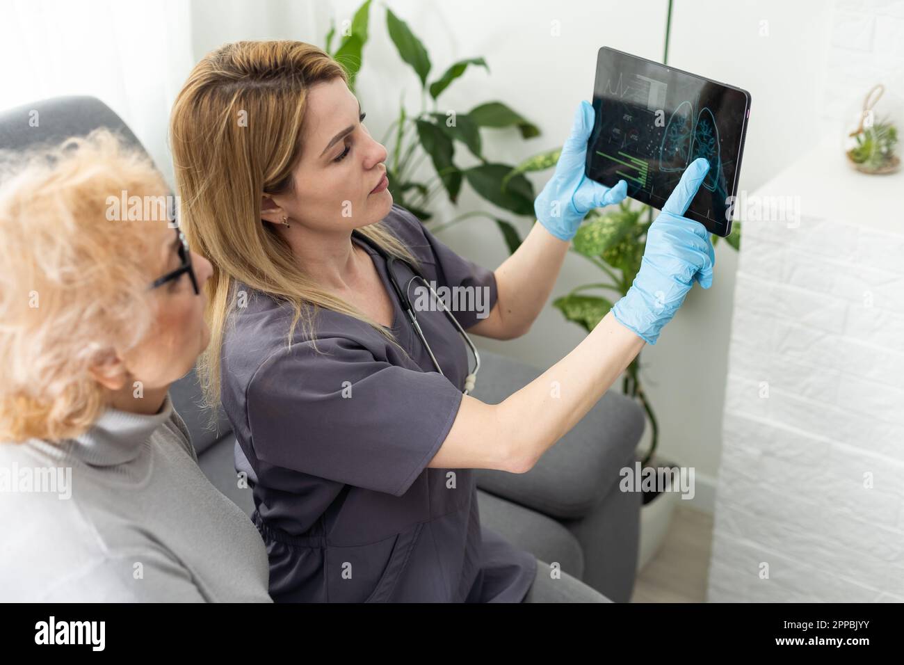Serious GP doctor showing tablet screen to old 70s female patient ...