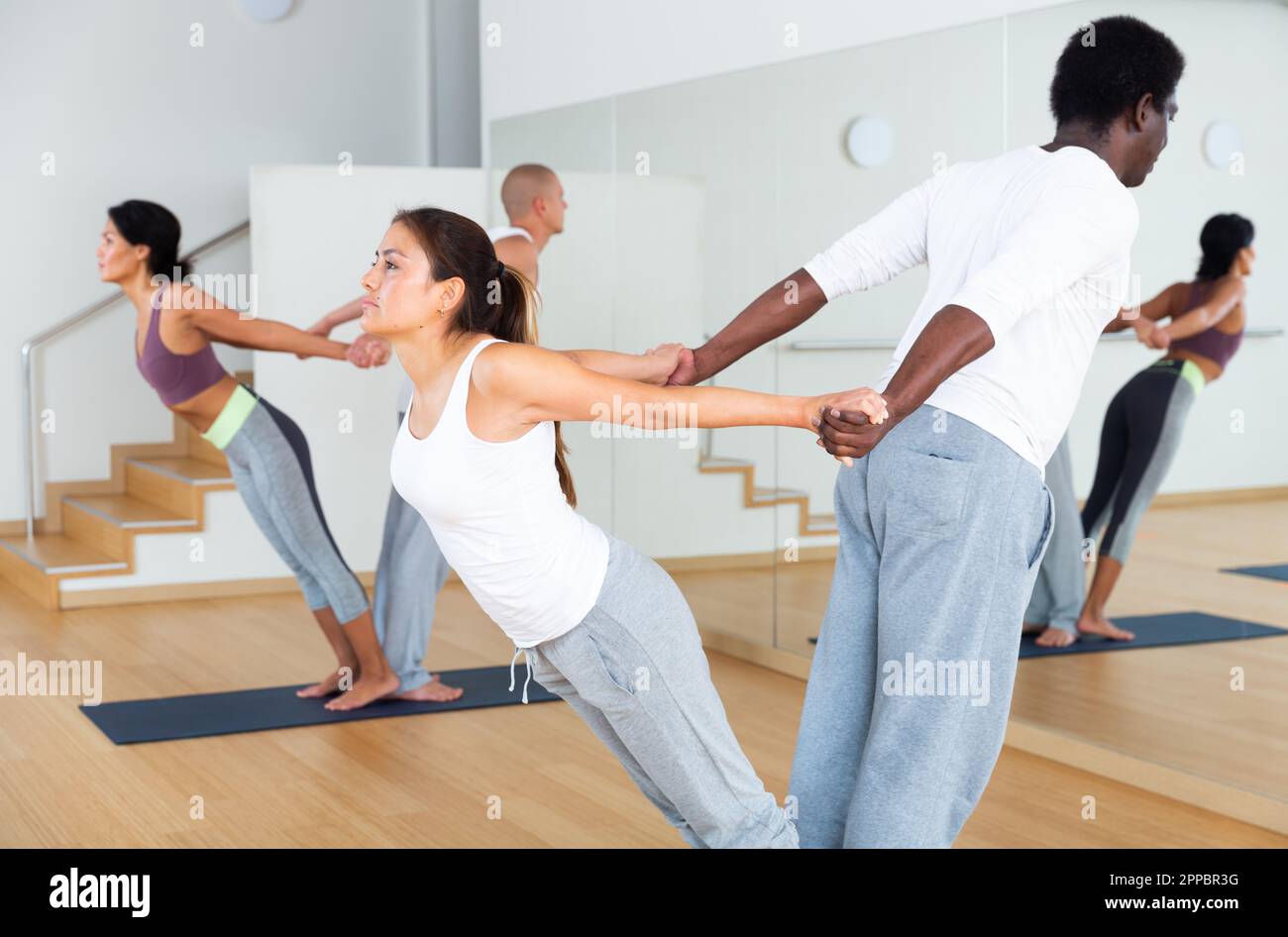 Women and men performing paired yoga exercises during group training ...
