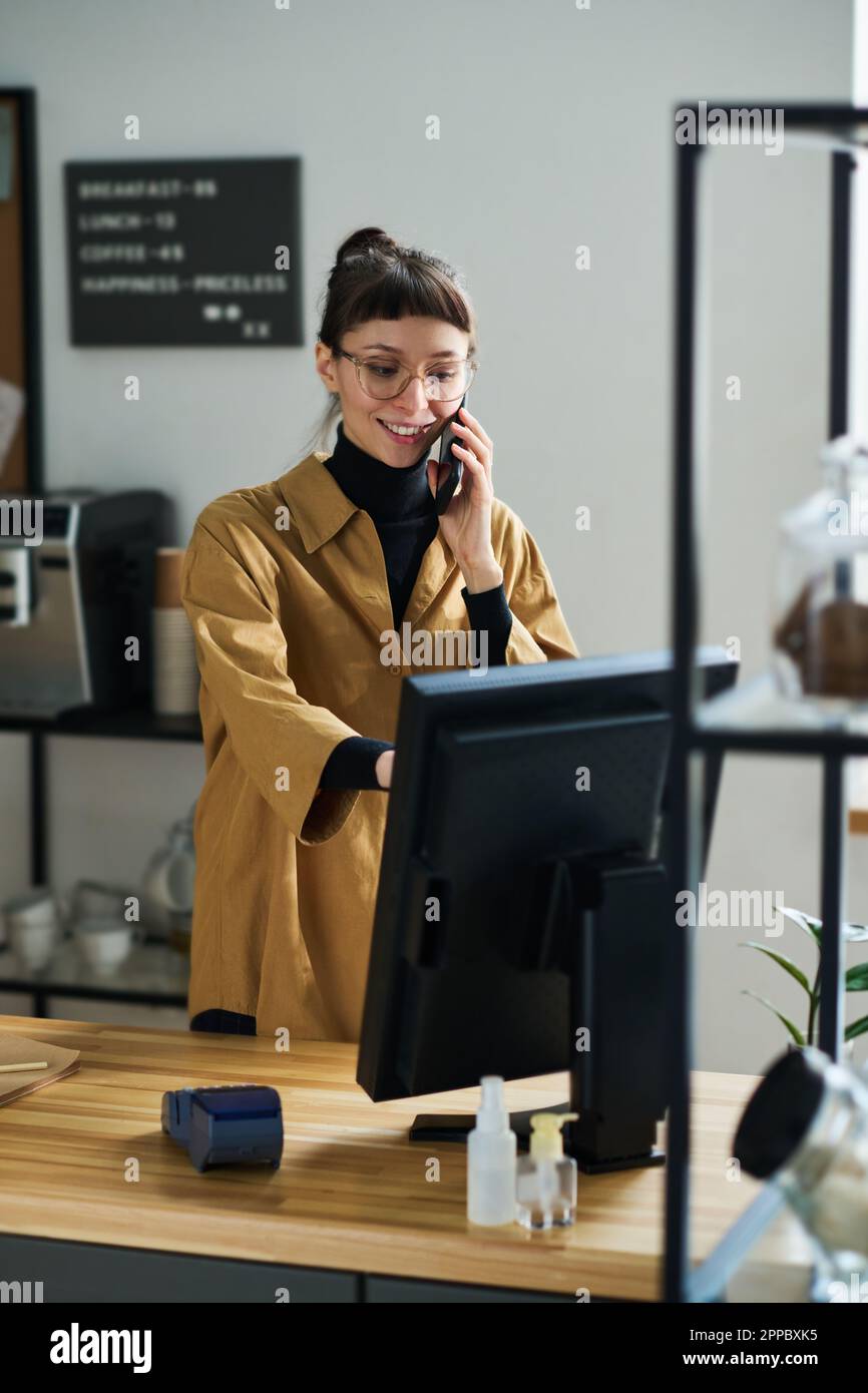 Happy young clerk with smartphone by ear taking order of client and ...