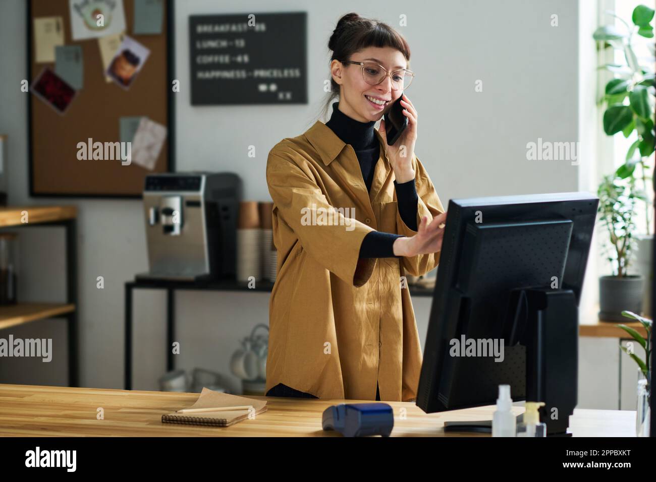 Young smiling female clerk talking with client on smartphone and ...