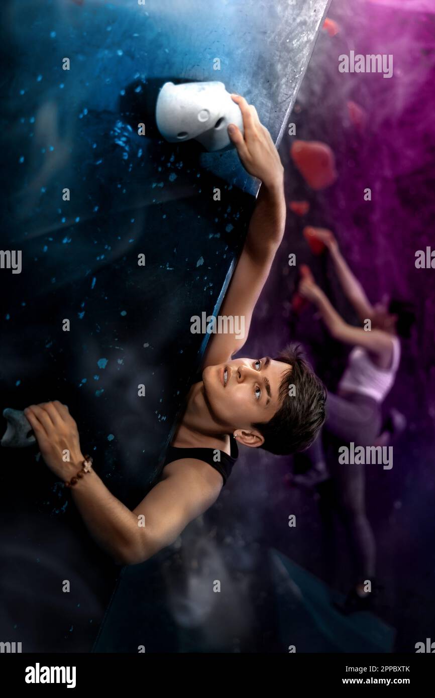 Positive focused young guy exercising on black climbing wall without ...