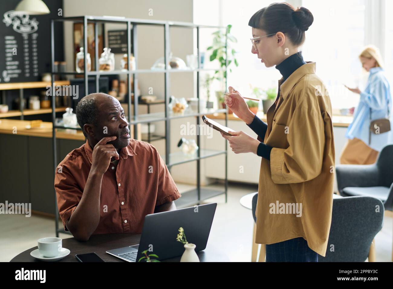 Side view of young waitress with notepad talking to African American ...